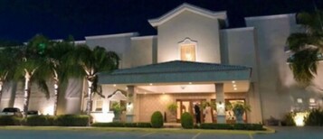 Um hotel com entrada central, alpendre coberto e palmeiras.