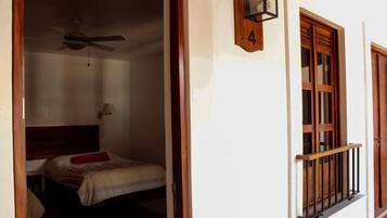 Quarto com cama, ventilador de teto e janela com moldura de madeira e grades de varanda.