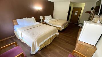 Quarto de hotel com duas camas, piso de madeira, escrivaninha com cadeira e um refrigerador.