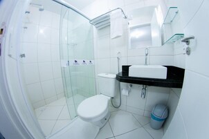 Uma casa de banho moderna com chuveiro em cabine de vidro, sanita branca, lavatório preto e um cesto de lixo de vidro.