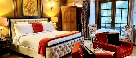 Quarto bem decorado com uma cama grande, um guarda-roupa de madeira e um espaço de estar com cadeiras vermelhas e uma mesa.