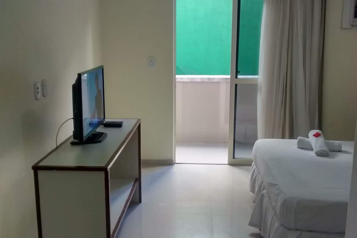 Quarto de hotel com cama, secretária com computador e porta de vidro deslizante para a varanda.