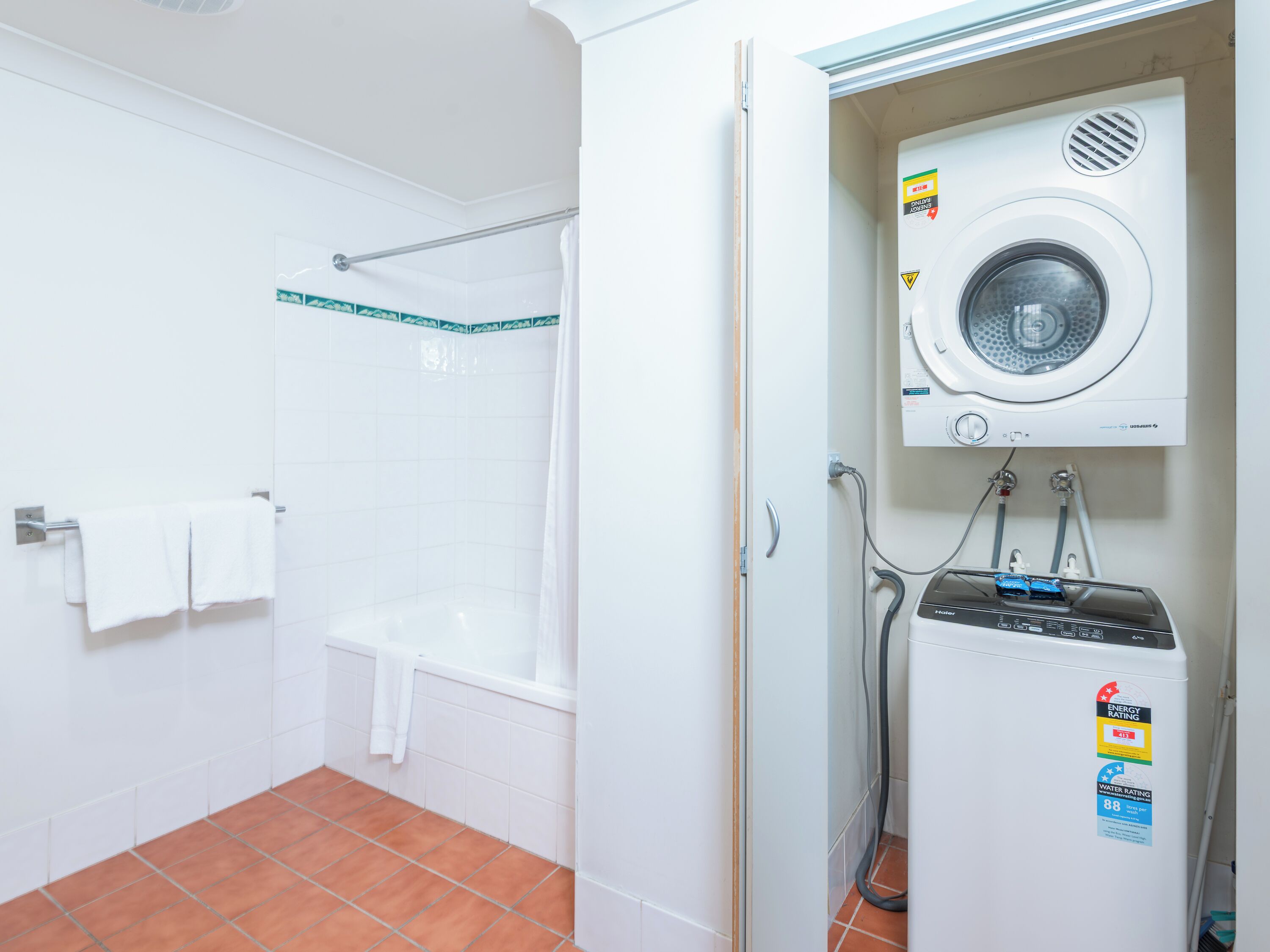Casa de banho com banheira branca, área de duche e máquina de lavar roupa encastrada na parede.
