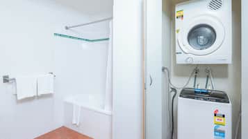 Casa de banho com banheira branca, área de duche e máquina de lavar roupa encastrada na parede.