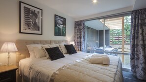Cama bem arrumada com cabeceira, abajur e duas fotos emolduradas na parede.