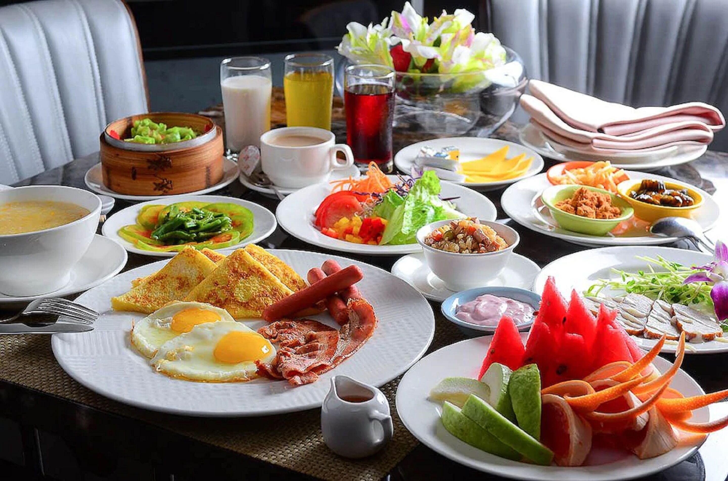 Um buffet de café da manhã com diversos pratos, incluindo ovos, bacon, torradas e frutas frescas.