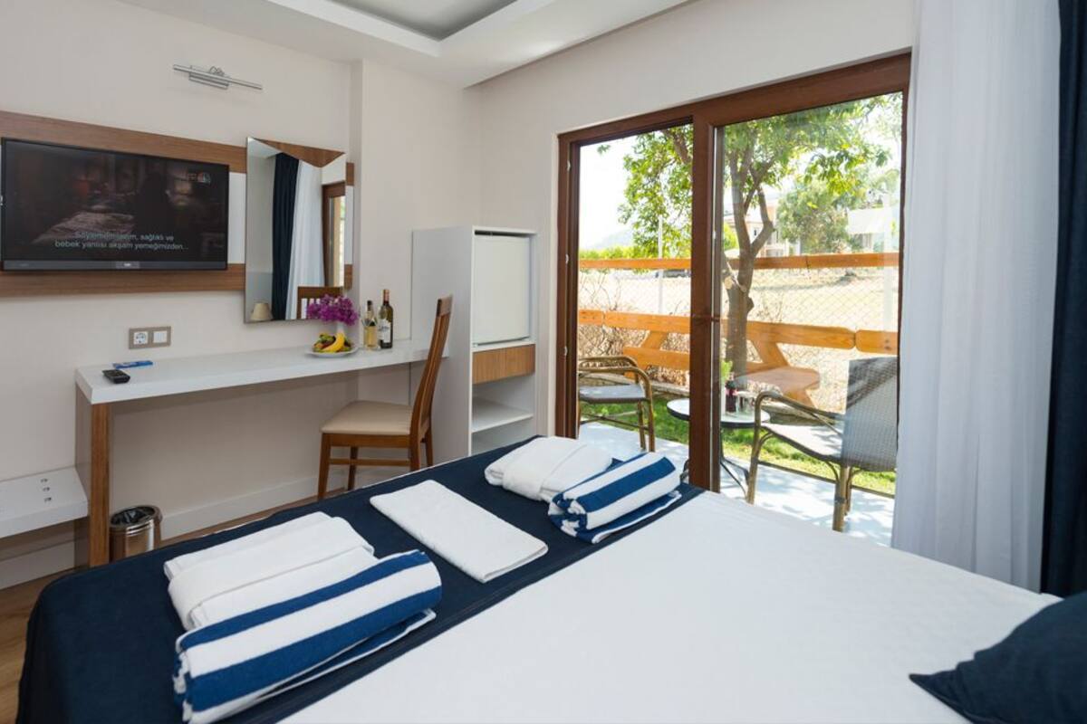 Quarto de hotel com cama, escrivaninha, cadeira, televisão e varanda com mobiliário exterior.