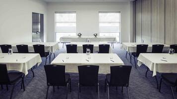 Sala de conferências com várias mesas e cadeiras, janelas amplas e design moderno no teto.