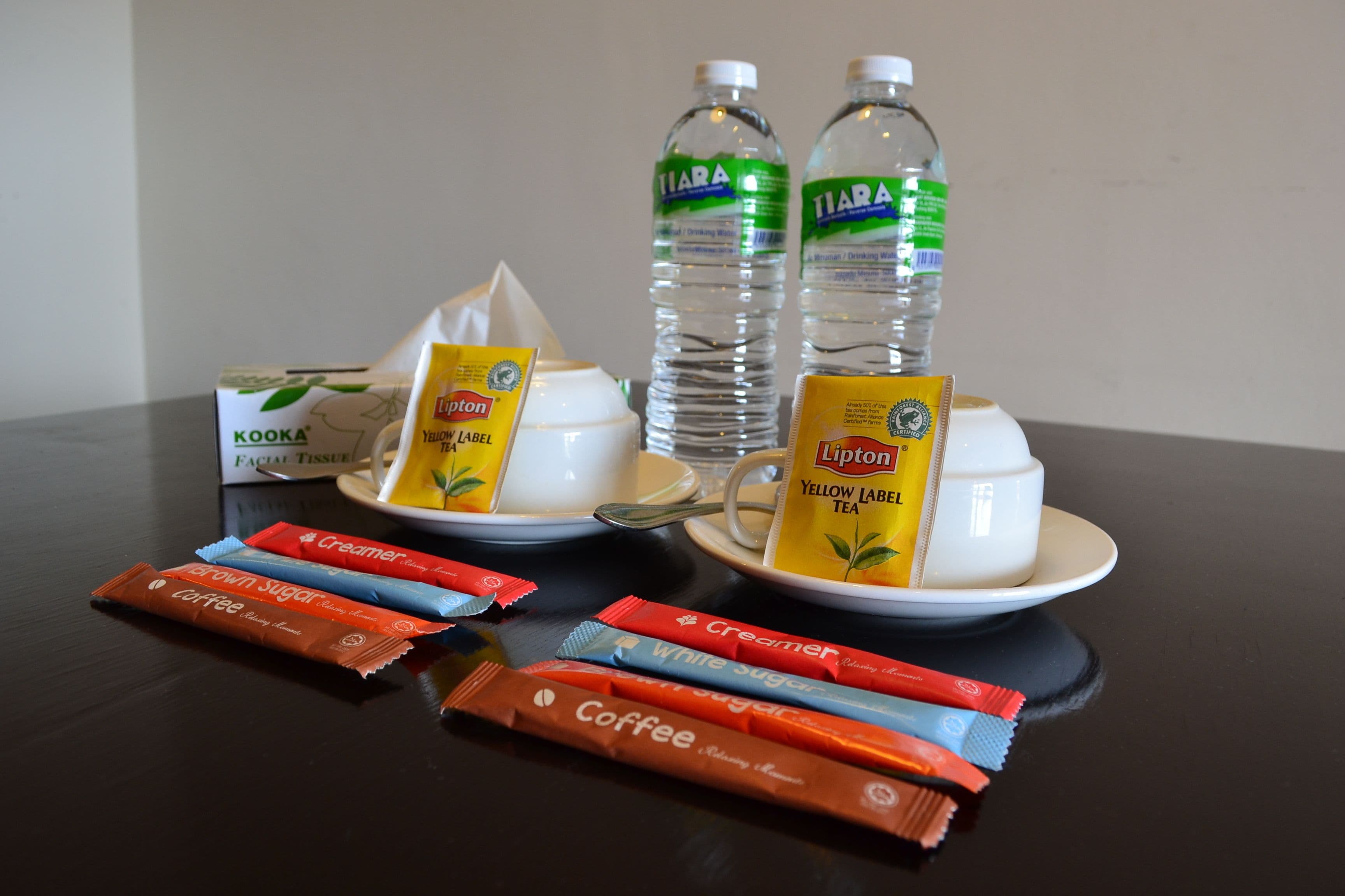 Uma mesa com duas chávenas de chá, duas garrafas de água e vários pacotes de café e leite.