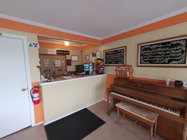 Uma área de recepção com balcão, piano, extintor de incêndio e um letreiro com a inscrição 'Masha Allah'.