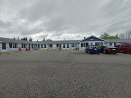 Um motel com estacionamento de cascalho, algumas cadeiras vermelhas e amarelas, e alguns carros estacionados na frente.