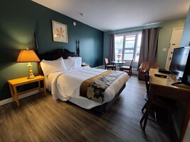 Quarto de hotel com cama, luminária, televisão, escrivaninha e janela com cortinas.