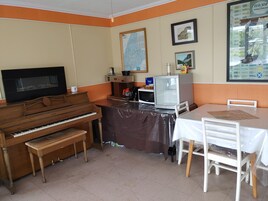 Quarto com piano, televisão, mesa com cadeiras e diversas fotos emolduradas na parede.