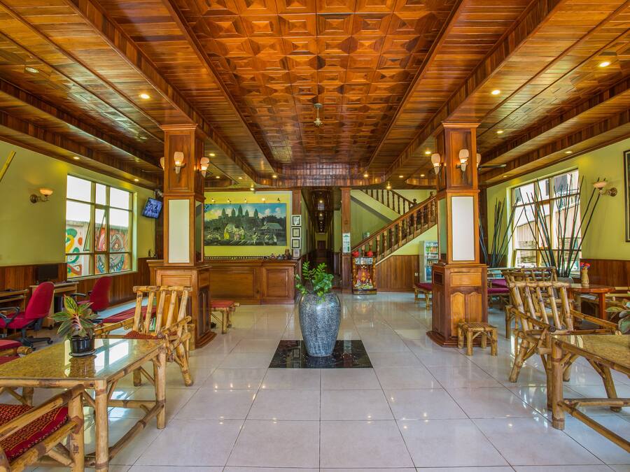 Um hall com teto de madeira, um vaso grande com plantas e uma escadaria.