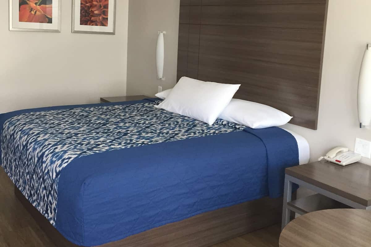 Quarto de hotel com uma cama grande, uma mesa de cabeceira e duas fotografias emolduradas na parede.