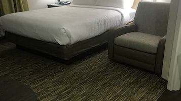 Quarto de hotel com cama, poltrona, escrivaninha e luminária.