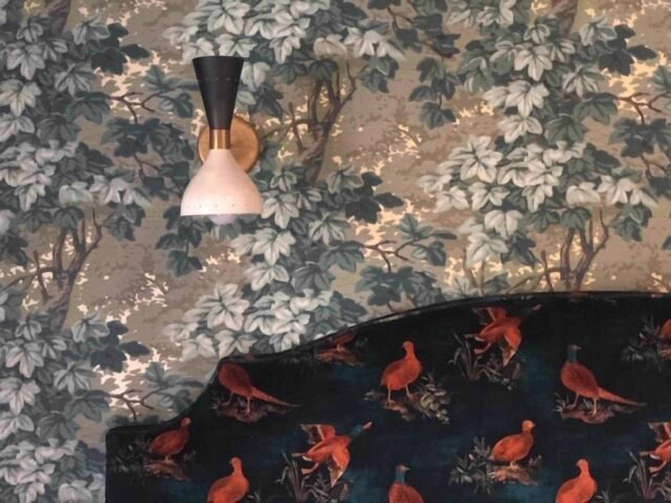 Um quarto com papel de parede estampado, um abajur pendente e tecido escuro com estampas de pássaros vermelhos.