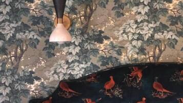 Um quarto com papel de parede estampado, um abajur pendente e tecido escuro com estampas de pássaros vermelhos.