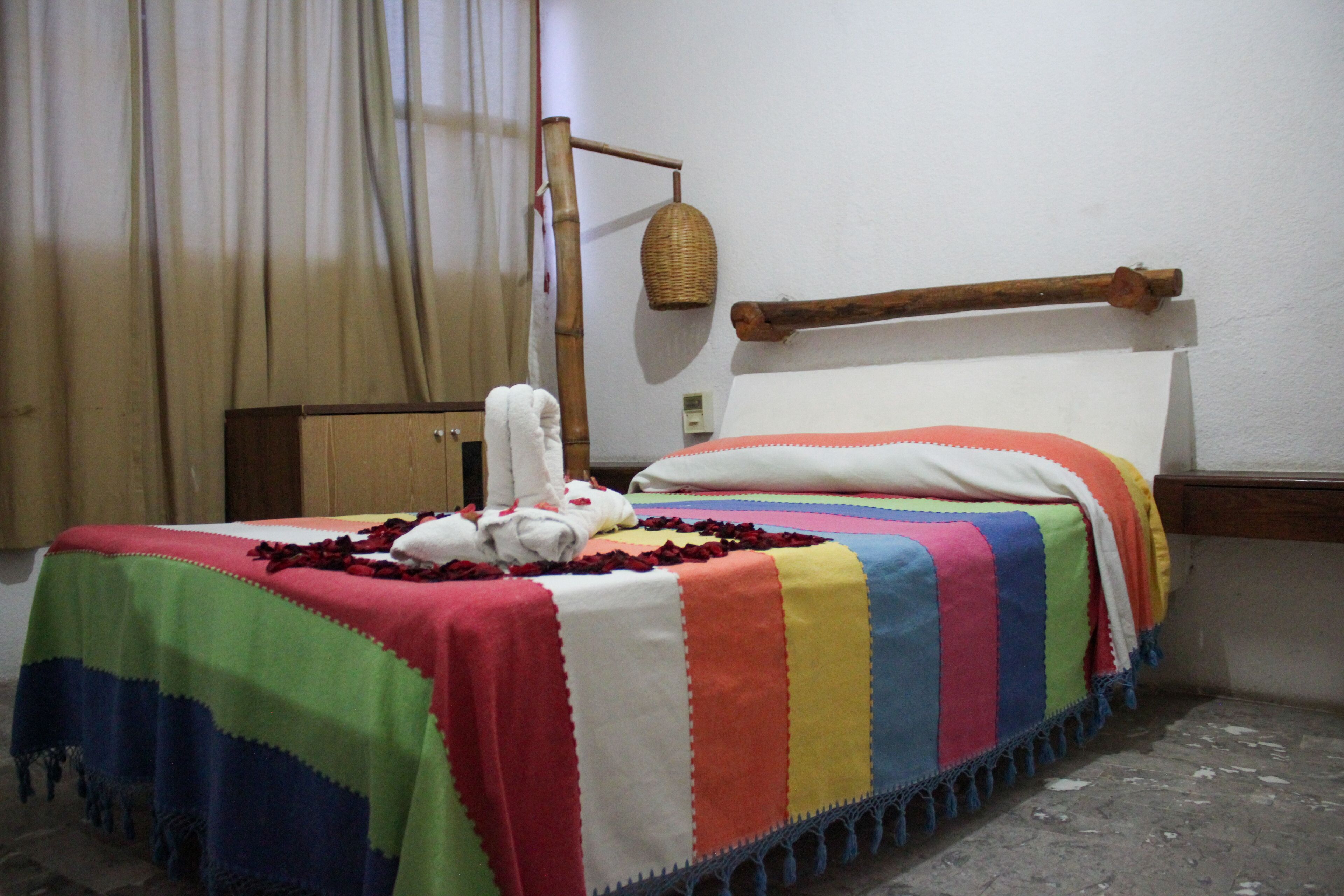 Cama com manta listrada e colorida, travesseiro e toalha brancos ao lado.