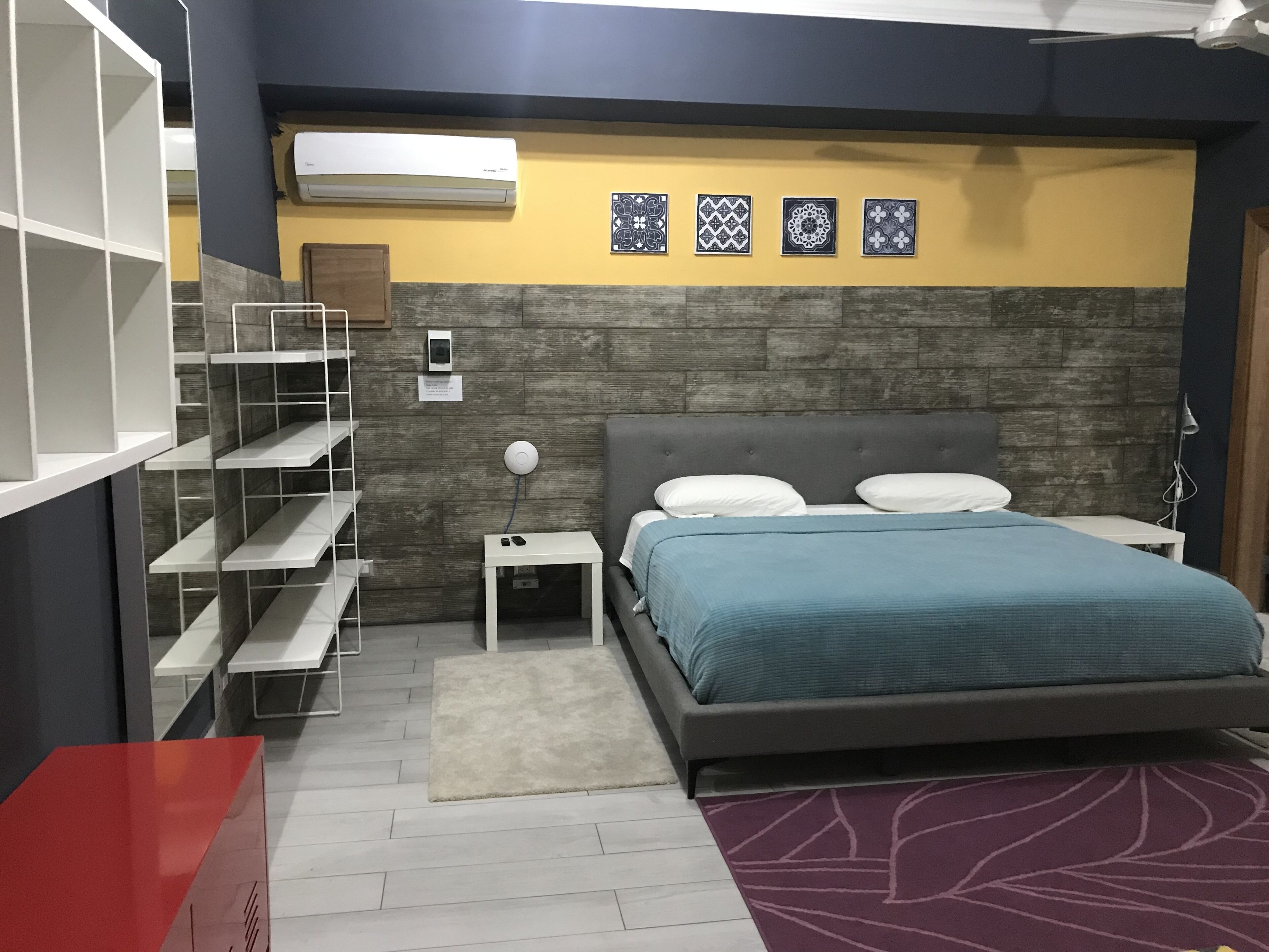 Quarto com cama, mesa de cabeceira, ar-condicionado fixado na parede e estante.