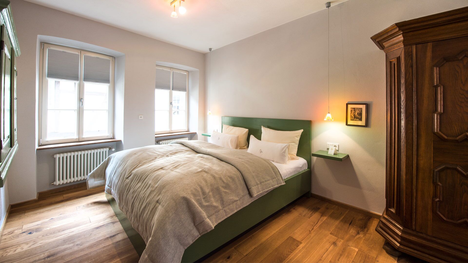 Quarto com cama, radiador, janela e guarda-roupa de madeira.