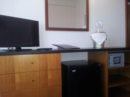 Quarto de hotel com secretária de madeira, televisão, cofre e minibar.