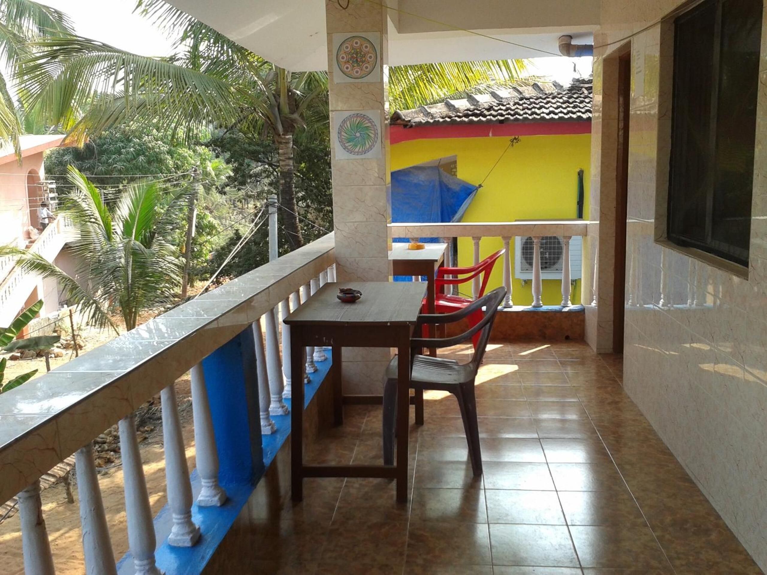 Uma varanda com mesa e cadeiras, guarda-corrimão azul e vista para o verde.