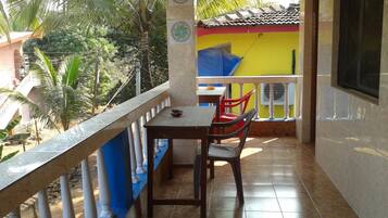 Uma varanda com mesa e cadeiras, guarda-corrimão azul e vista para o verde.