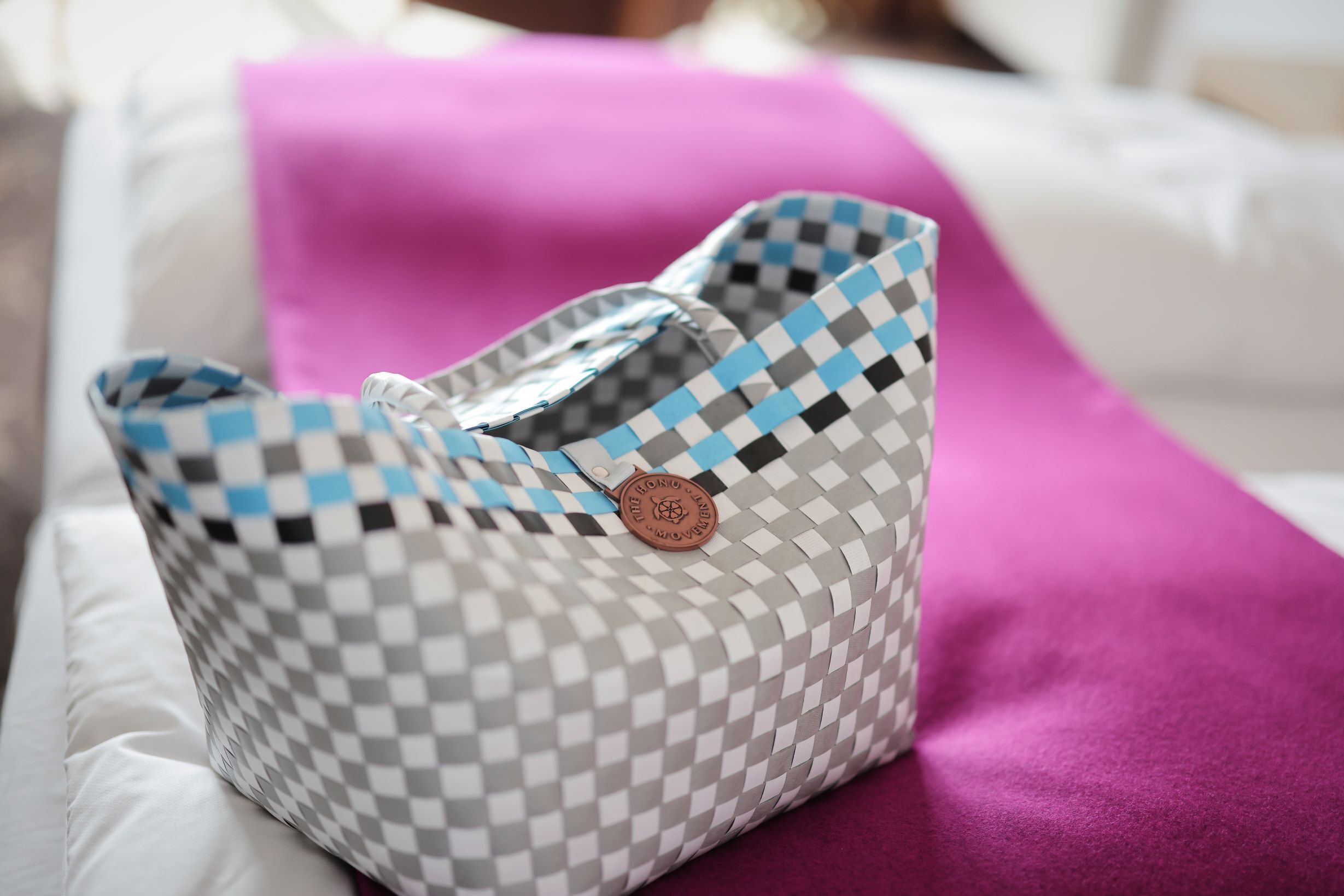 Uma bolsa xadrez com fecho de metal sobre um sofá branco com almofada rosa.