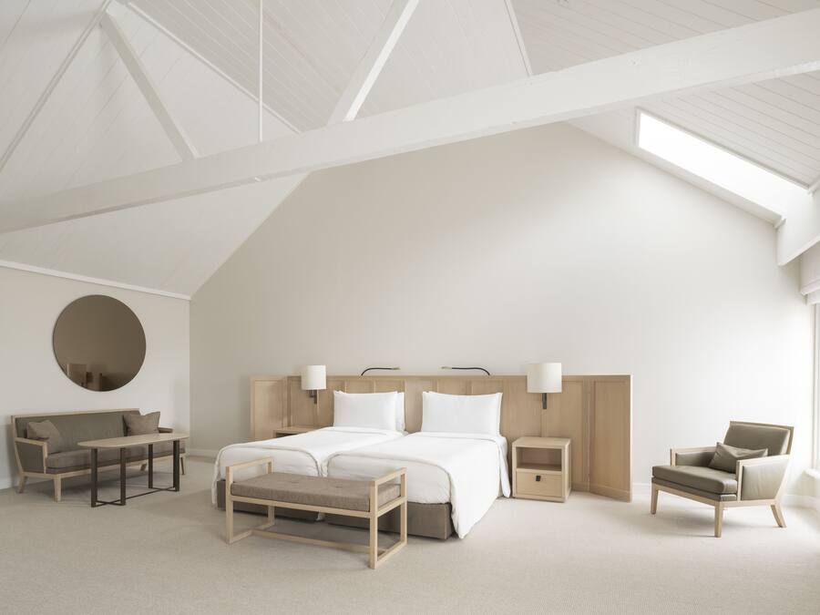 Quarto espaçoso e moderno com cama grande, sofá, poltrona e espelho redondo.