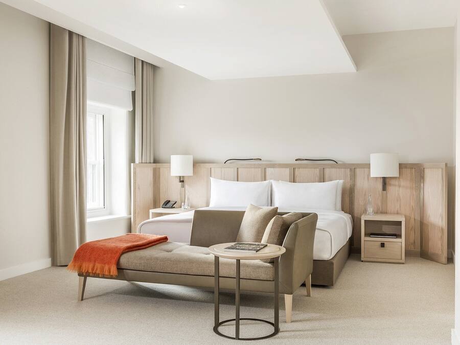 Quarto de hotel com cama, mesas de cabeceira, um sofá e uma pequena mesa redonda.