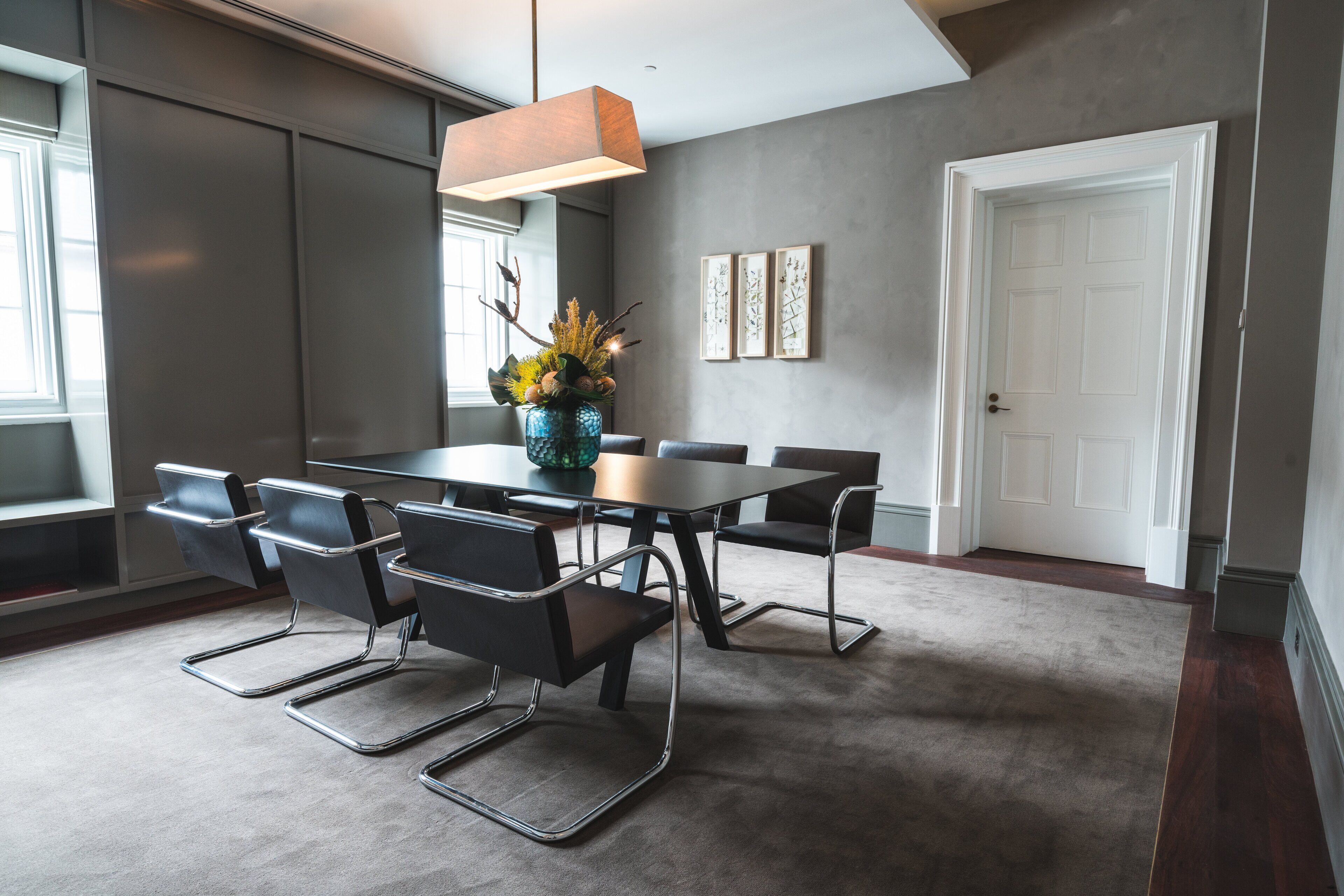 Uma sala de conferências moderna, com uma mesa grande, cadeiras pretas e um vaso com flores.