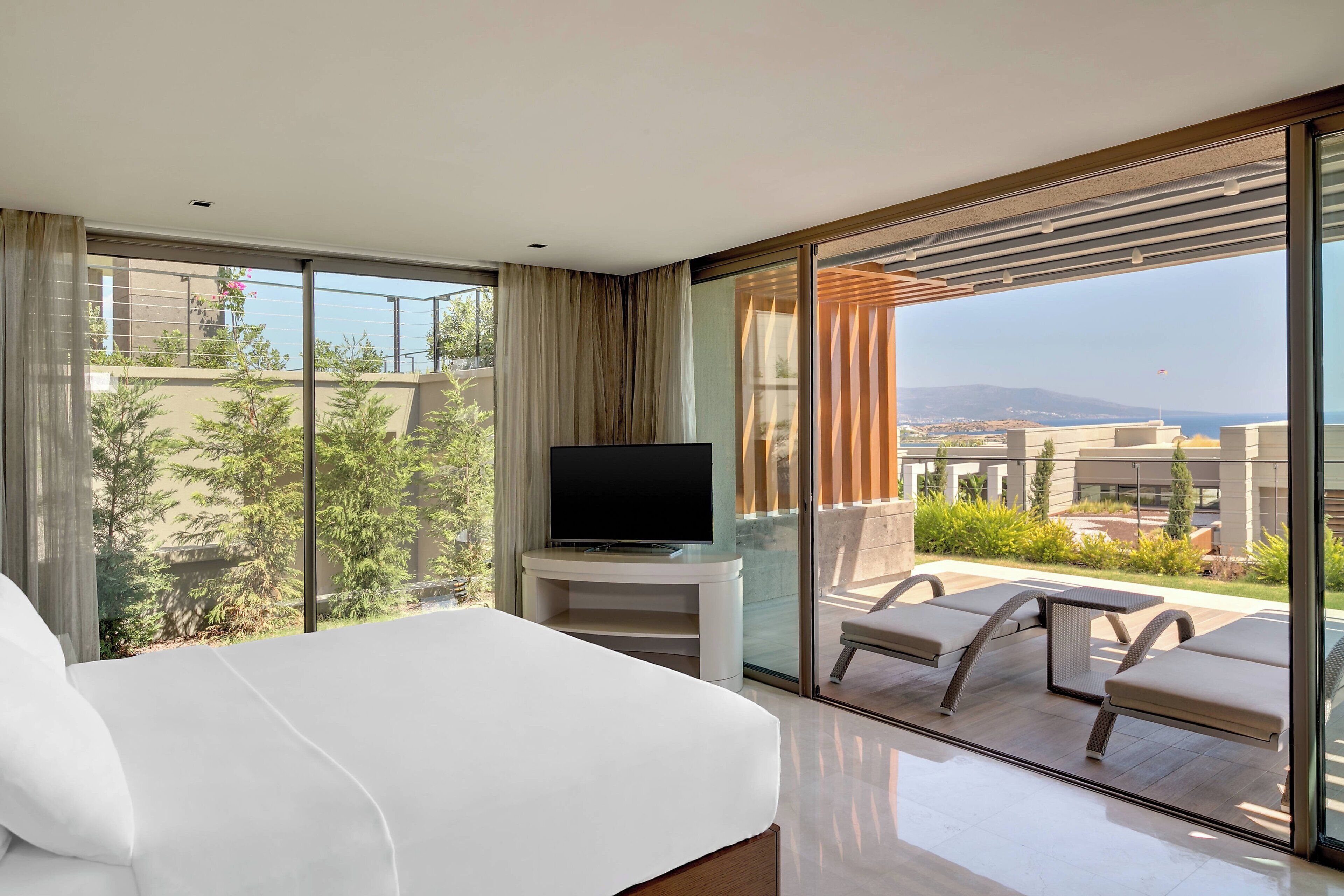 Quarto de hotel moderno com uma cama grande, televisão e varanda com área de estar.