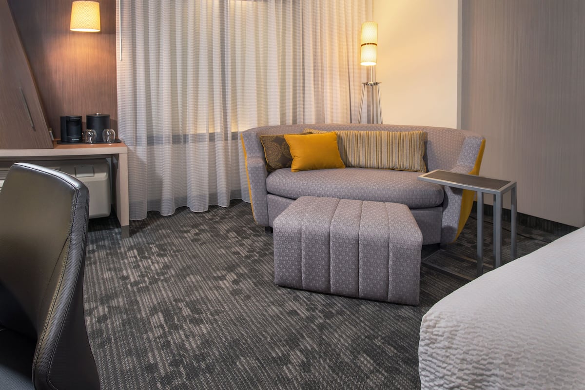 Quarto de hotel com sofá, apoio para os pés, escrivaninha e luminária.