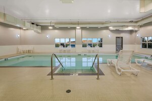 Piscina interna com água cristalina, rodeada por espreguiçadeiras brancas e piso revestido de azulejos.