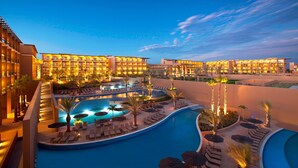 Um hotel com várias piscinas, espreguiçadeiras e palmeiras.