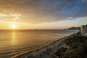 Uma praia com um pôr do sol, mar calmo e um navio ao longe.