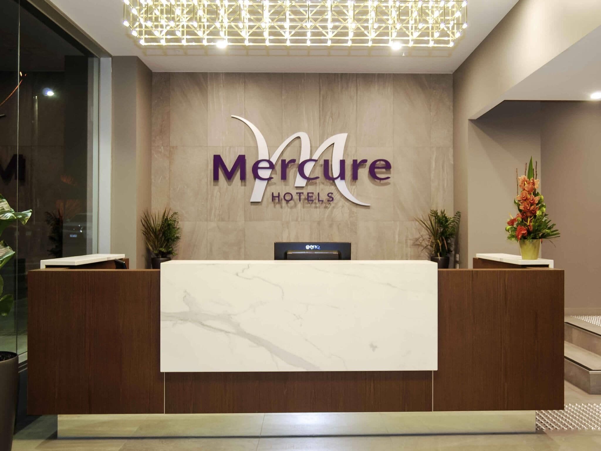 Um balcão de recepção de hotel com tampo de mármore, um candelabro moderno e uma placa com a inscrição 'Mercure Hotels'.