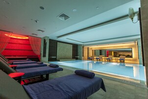 Uma área de piscina interior moderna, com espreguiçadeiras e um balcão de recepção.