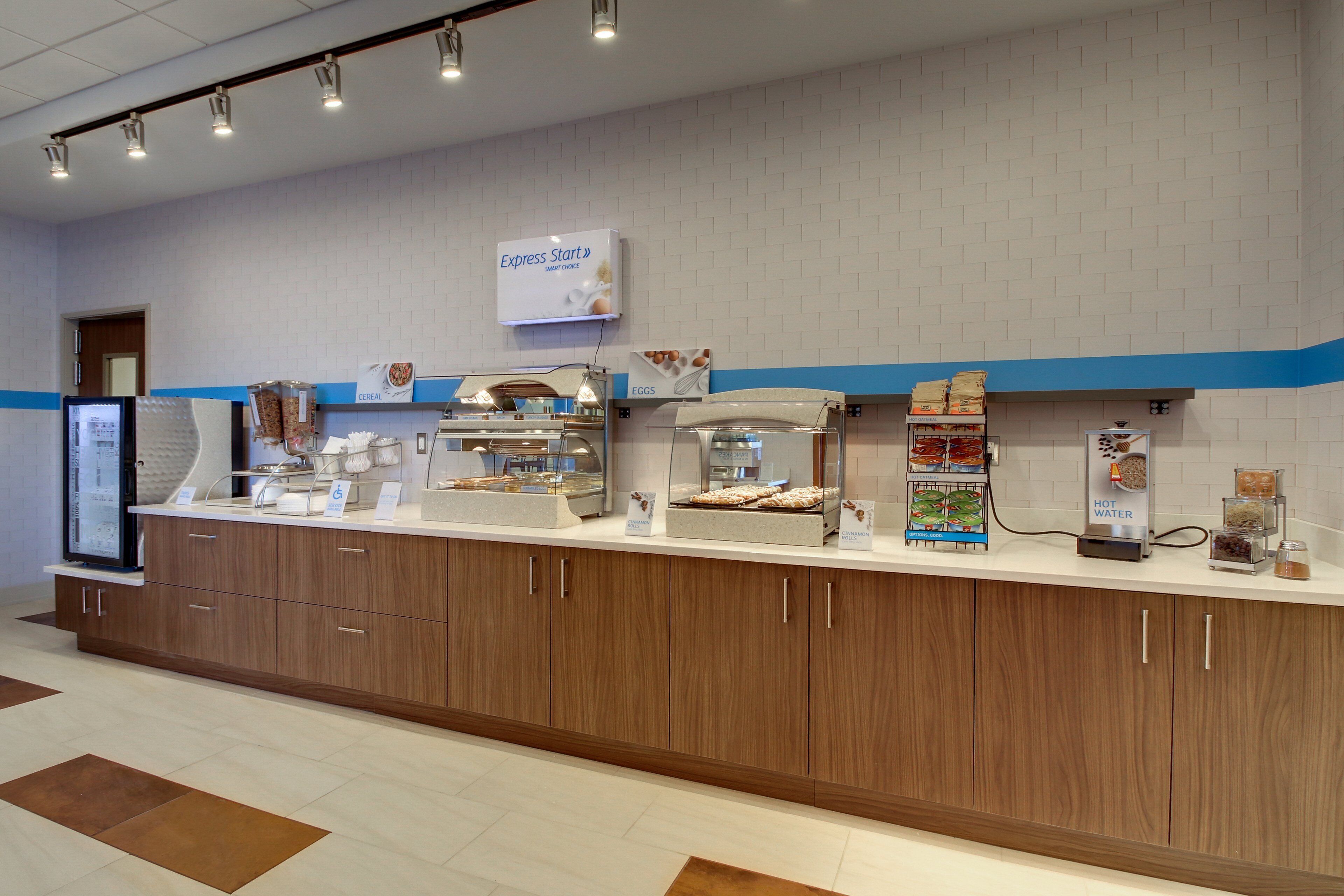 Uma área de buffet com um aviso para 'Express Start' (cereal), um dispensador de água quente e vários pontos de comida, incluindo ovos e cereal.