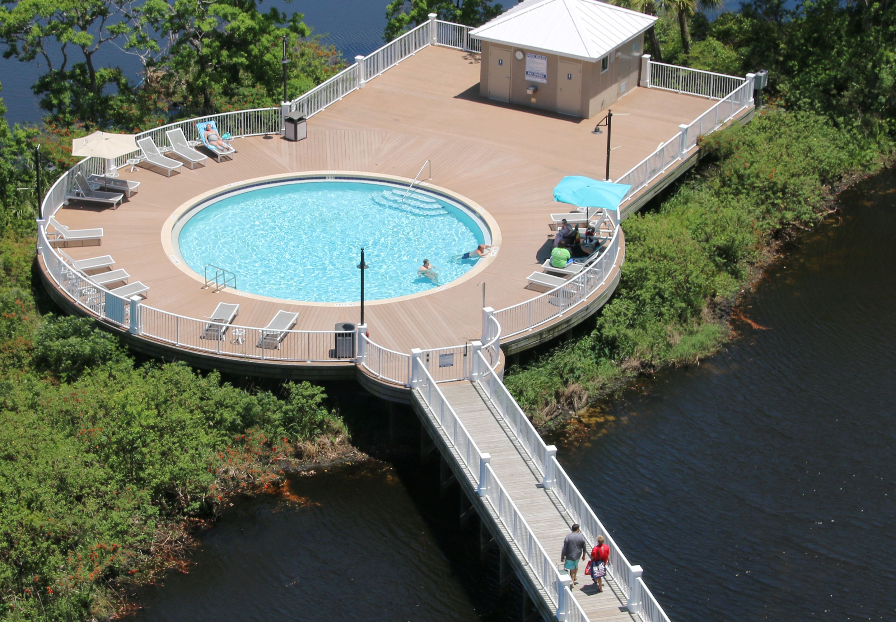 Piscina circular com um deck, rodeada por espreguiçadeiras e um pequeno edifício.