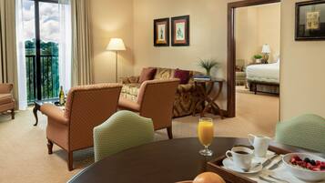 Quarto de hotel com varanda, uma mesa de jantar com itens de café da manhã e um sofá.