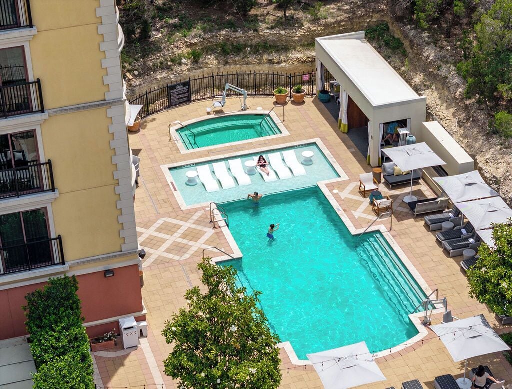 Piscina no terraço com várias pistas de natação, espreguiçadeiras e um pequeno edifício com fachada branca.