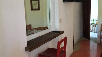 Quarto com cadeira vermelha, mesa pequena, espelho e televisão na parede.