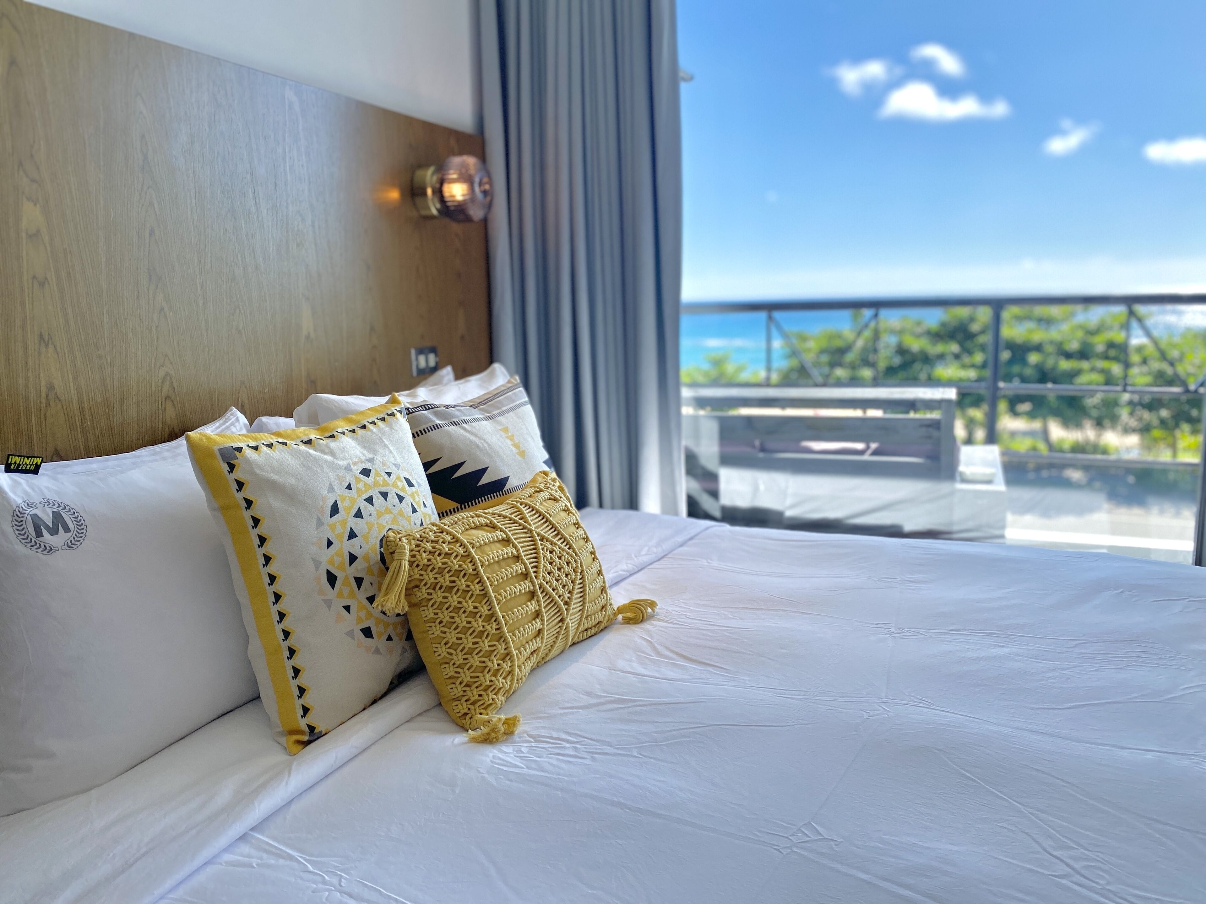 Quarto de hotel com cama, almofadas e vista para o oceano.