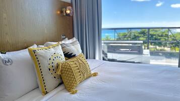 Quarto de hotel com cama, almofadas e vista para o oceano.