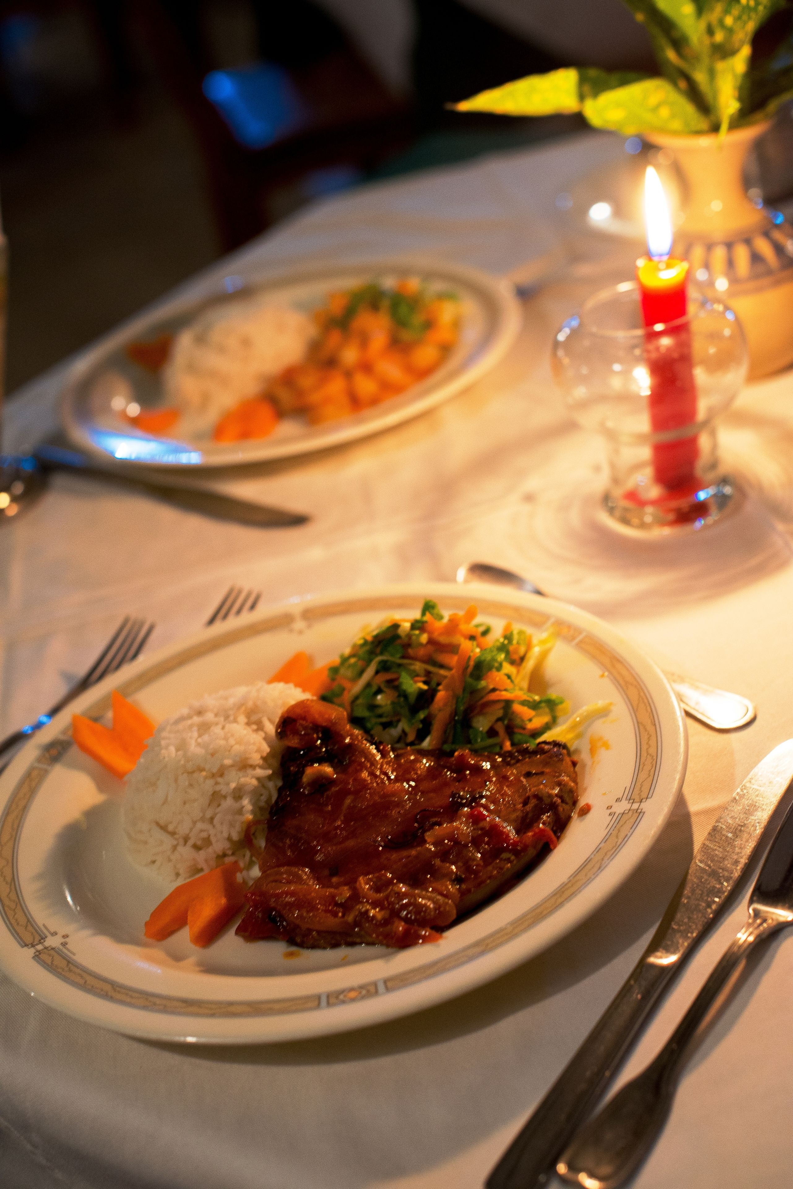 Uma mesa de jantar com pratos de comida, utensílios e uma vela acesa.