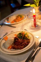 Uma mesa de jantar com pratos de comida, utensílios e uma vela acesa.