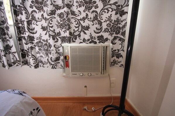 Quarto com uma cama, ar condicionado fixado na parede e janela com cortinas.