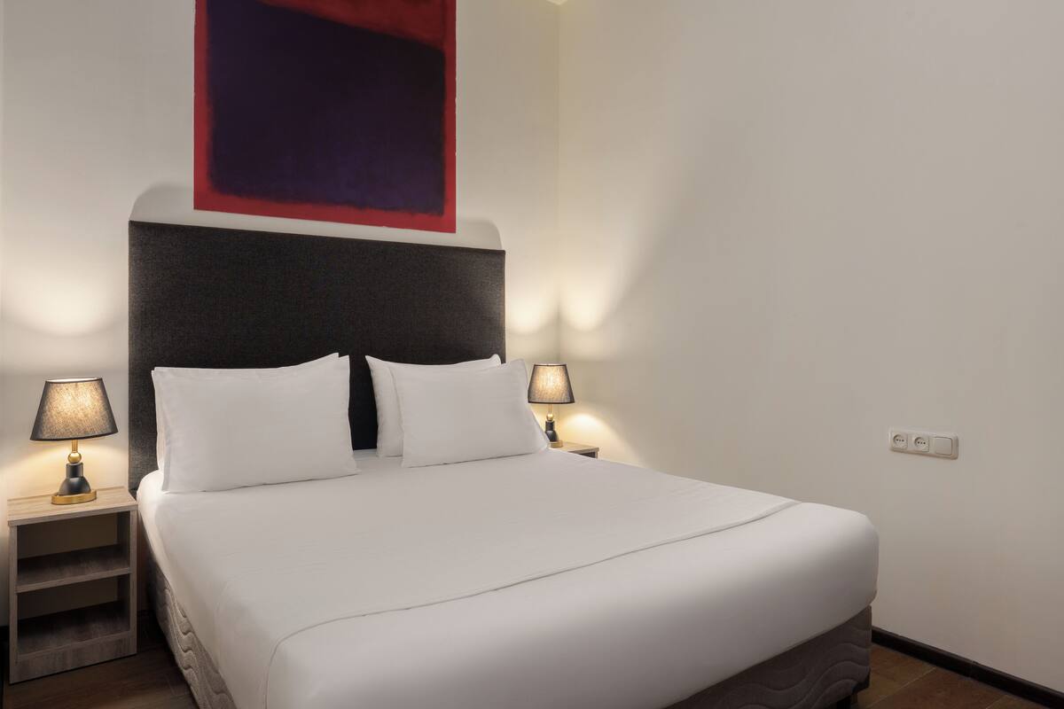 Cama bem arrumada com duas almofadas, uma luminária de cabeceira e mesa de cabeceira.